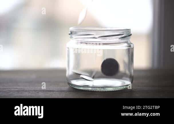 Ukrainian coins falling into the glass jar on wooden table near window ...