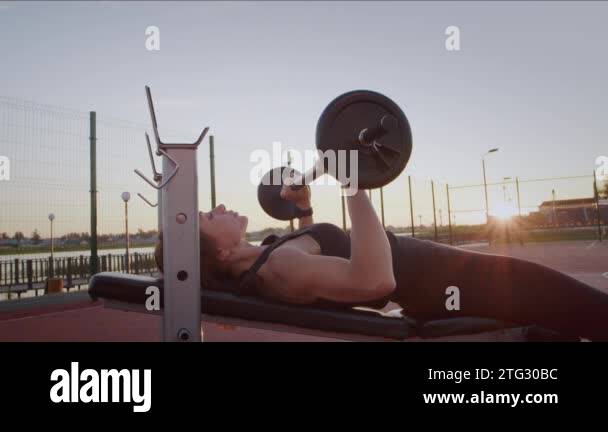 Sportive woman builds up muscles lifting heavy barbell on training ...