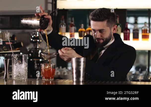 Professional barman in black suit standing behind counter and pouring ...