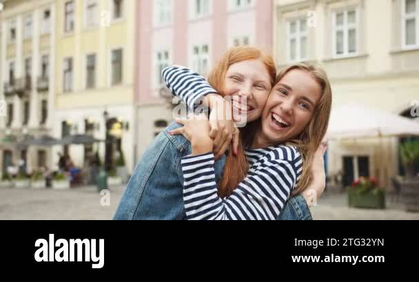 Two young women girls hugging, cuddling, looking to camera on street in ...