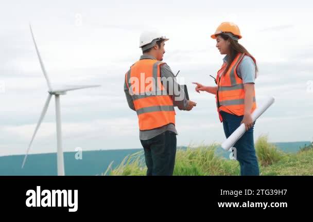 Male and female engineers working on a wind farm atop a hill or ...