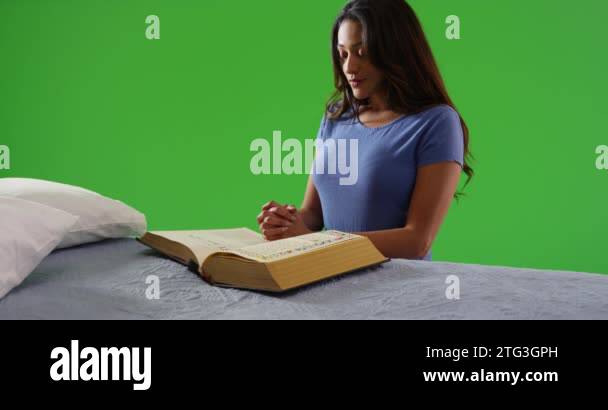 Young Latina woman sitting in her bedroom praying with open bible on ...