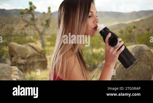 Side view of millennial woman drinking water from bottle in desert ...