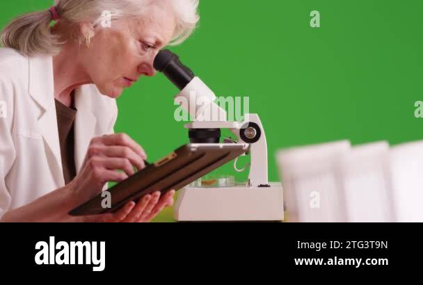 Scientist examining substance through microscope writing down info ...