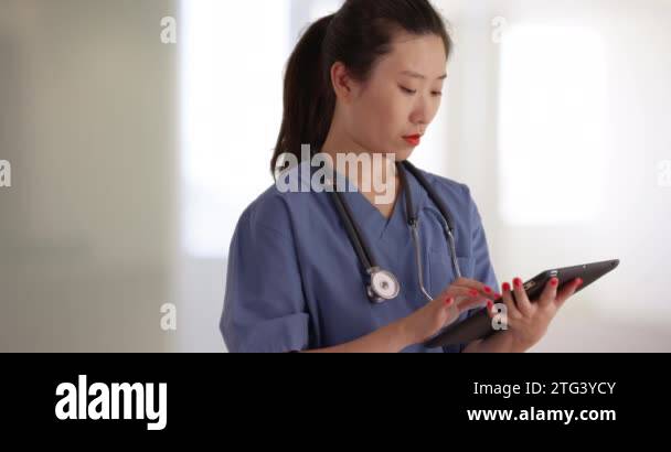 Working millennial nurse dressed in scrubs using handheld tablet device ...