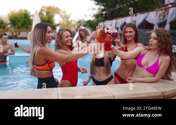 Girls in bikini have pool party with cocktails in swimming pool. Women relaxing clinking glasses ...