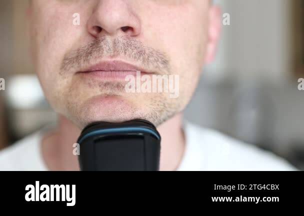Handsome young unshaven man shaving with modern electric razor trimer ...