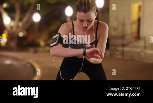 Woman runner using smartwatch fitness tracker while running at night in ...