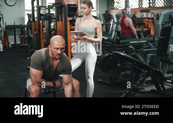 Female attractive slim personal trainer coordinating a weight training ...