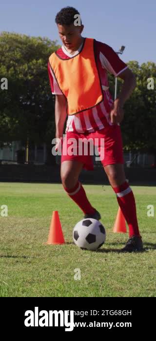 Vertical video of biracial football player on field kicking ball. Male ...