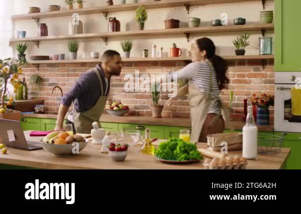 Excited man and his wife have a good time in the kitchen dancing and ...
