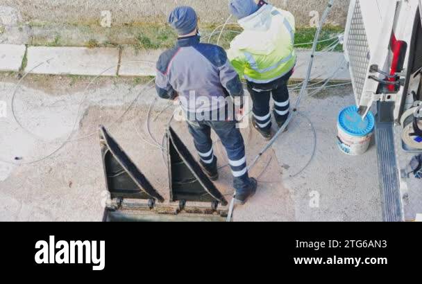 Workers insert fiber optic cables into the underground cable ducts to ...