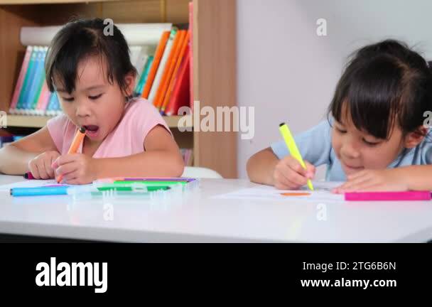Little girl coloring with her friends sitting in the classroom. Two ...