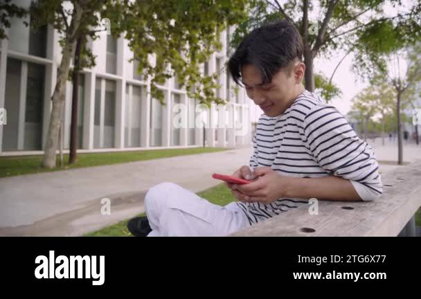 Funny Asian guy at university campus sitting on a bench chatting with a ...