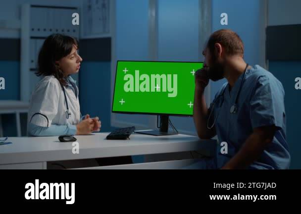 Medic and assistant looking at computer monitor with green screen ...