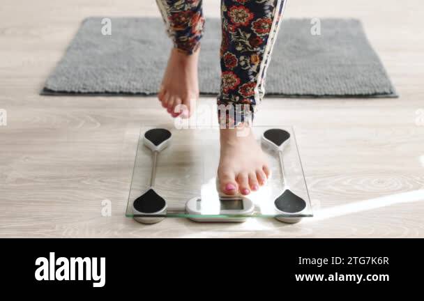 Female feet step on floor scales close up. Woman measuring her body ...