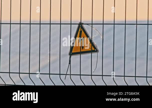 High voltage sign on a wire fence of the solar plant. Yellow triangular ...