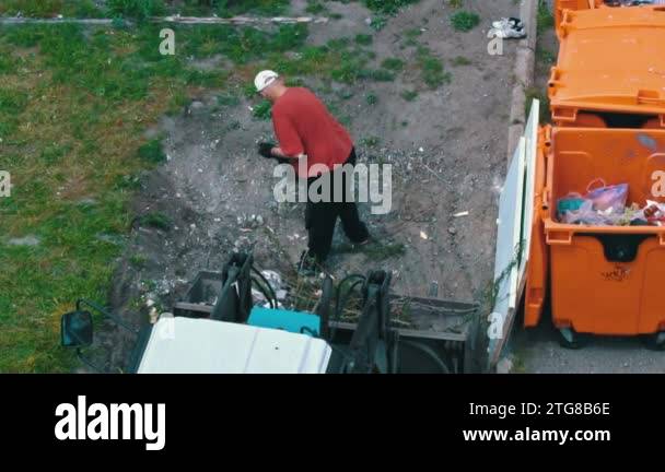 Man with a shovel loads garbage into a tractor tank. The garbage truck ...