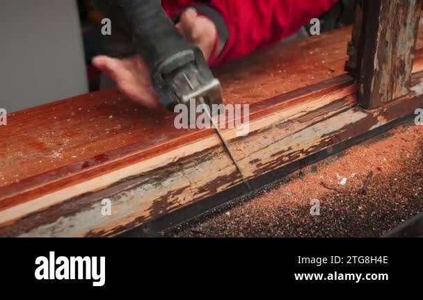 Worker cutting and dismantling old window frame using electric hand saw ...