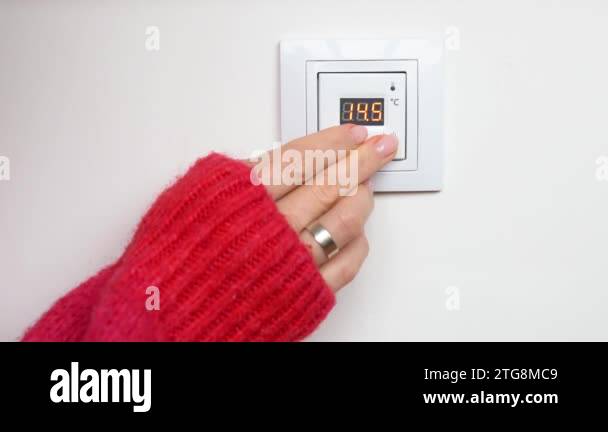 Woman hand in a red sweater setting temperature on underfloor heating ...
