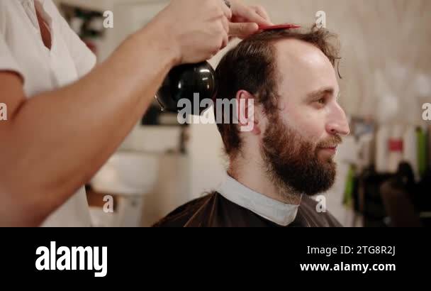 Attractive male is getting a modern haircut in barber shop. Barber sets ...