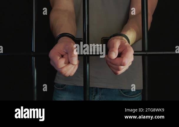 A convicted man is handcuffed in a cell behind bars on a dark ...