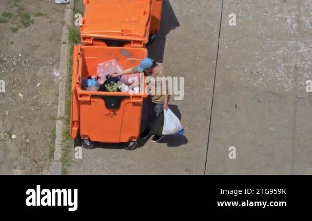 Homeless man rummages through the garbage can and looks for food and ...