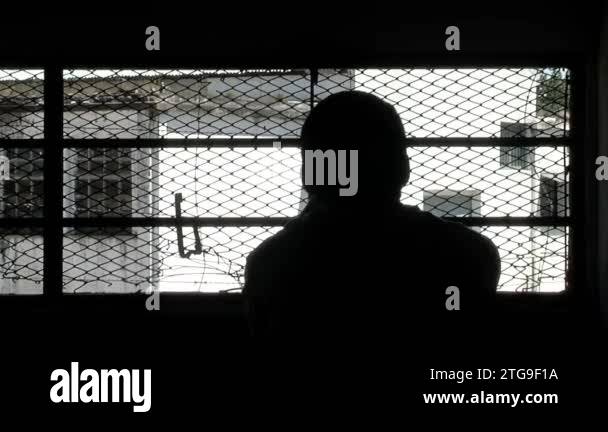 Silhouette of an Inmate Looking Through Window Bars inside a Cell of An ...