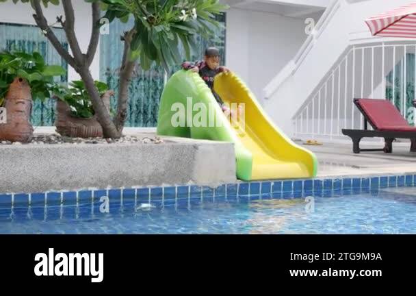 Asian child little boy playing outdoor swimming pool on water slider bar toy, Happy kid playing ...