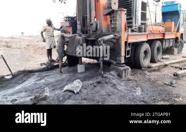 A laborer is tying the borewell drilling pipe with a rope and getting ...