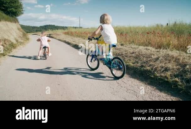 Carefree children ride bicycle on country road along the agricultural ...