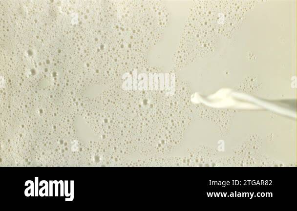 A stream of milk flows with splashes and air bubbles. On a white ...