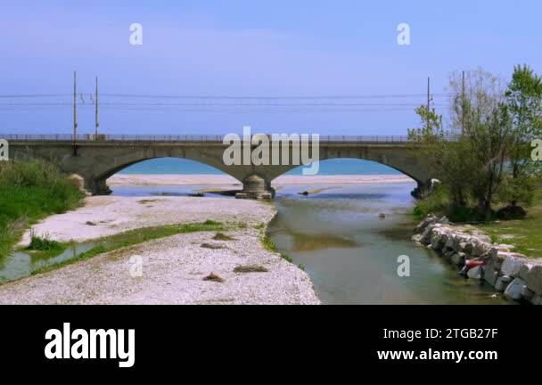 On a sunny morning in Italy, a stream of clear water at the mouth of a ...