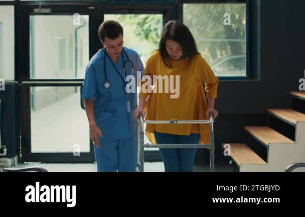 Female nurse helping patient with leg injury to use walk frame, dealing with physical impairment ...