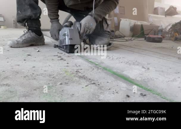 A man makes recesses in the concrete floor for installing underfloor ...