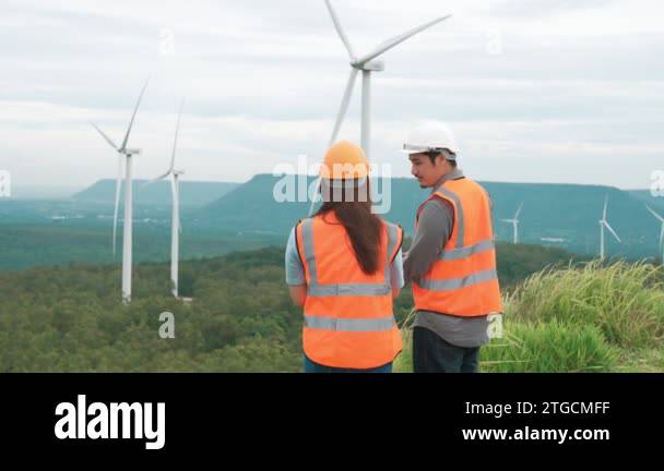Male and female engineers working on a wind farm atop a hill or ...