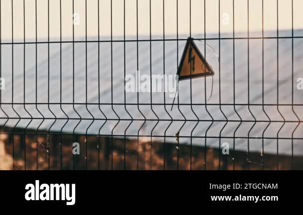 High voltage sign on a wire fence of the solar plant. Yellow triangular ...