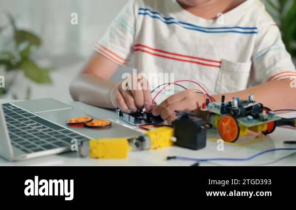 Asian kid boy plugging energy and signal cable to sensor chip with Arduino robot car, Little ...