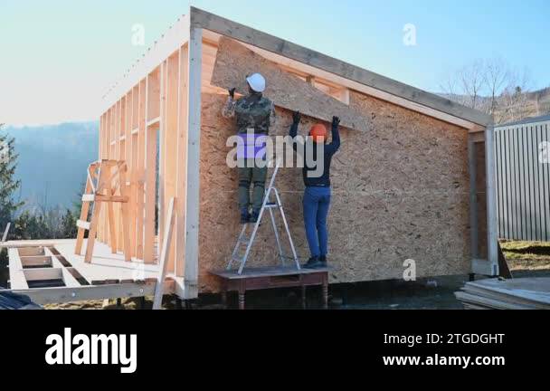 Carpenters mounting wooden OSB board on the wall of future cottage. Men ...