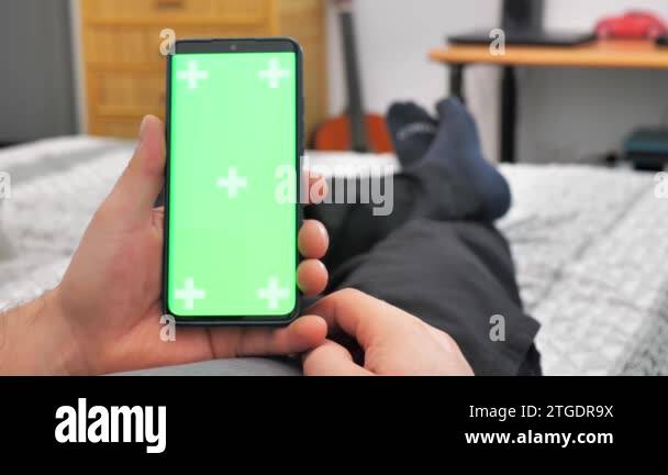 Man lying on couch using smartphone with chroma key green screen at night, scrdoing various ...