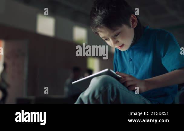 Excited playful teen boy playing online game holding tablet in school ...
