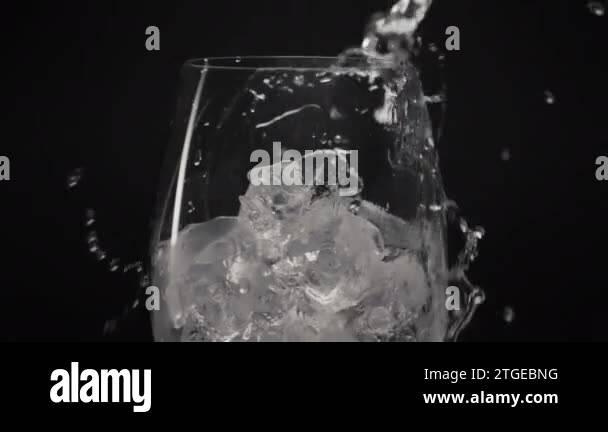Cold ice cubes drink glass closeup. Clear splashed water pouring in transparent wineglass slow ...