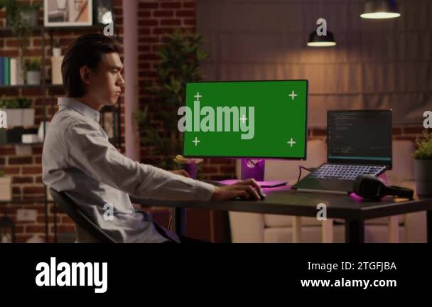 Asian businessman looking at computer with greenscreen on display, analyzing isolated copyspace ...