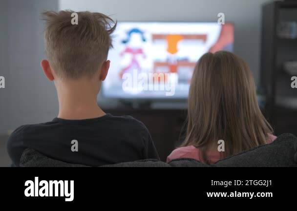 Rear view of brother and sister watching TV at home. Children sitting ...