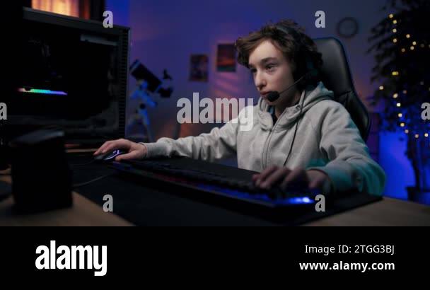 Focused young boy sits in front of computer with headset, child plays ...