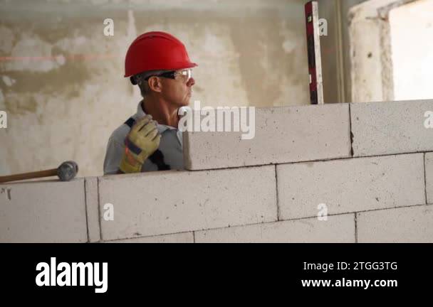 Bricklayer using rubber mallet hammer to tap, level concrete blocks ...