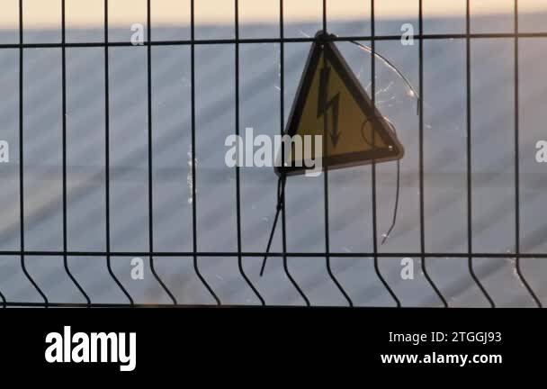 High voltage sign on a wire fence of the solar plant. Yellow triangular ...