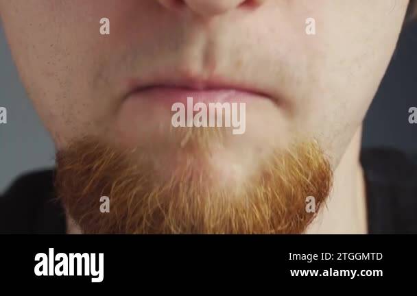 A young man in a black jacket and with a red beard eating gummy in the ...