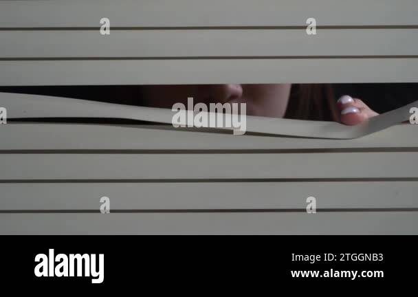 Close up front portrait from indoors of young girl pushing blinds at ...