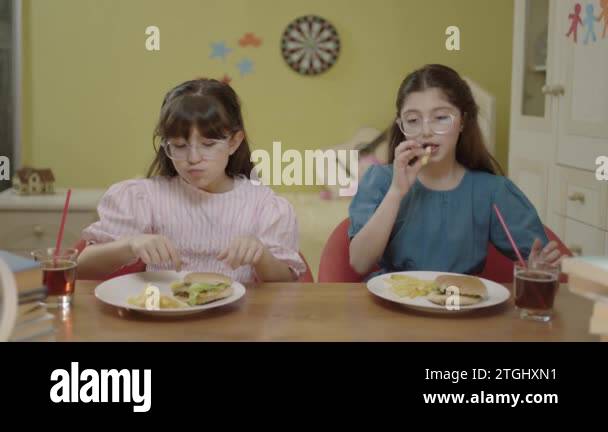 Little girls doing school homework are eating hamburgers. Little kids ...